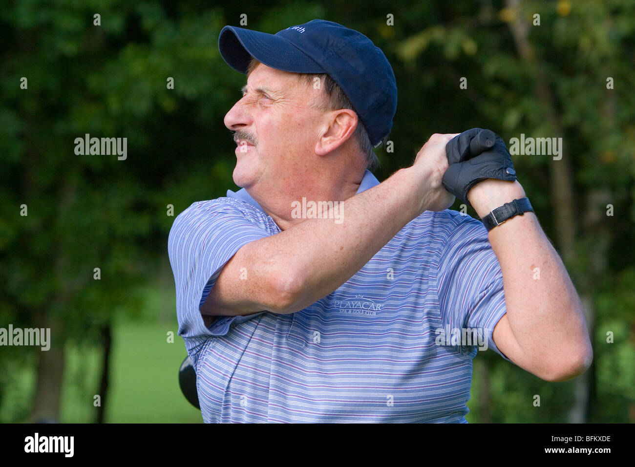 A middle aged white male playing golf watching his ball after teeing ...