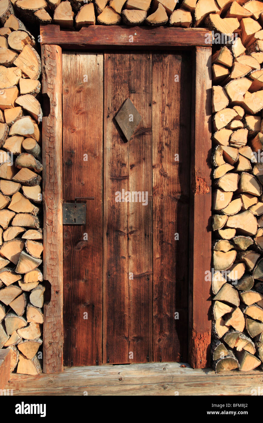 stacked firewood and wooden door entrance at the wall of a barn. Photo ...