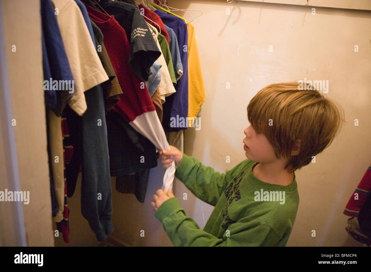 child trying to pull a shirt off of a hanger in bedroom closet Stock ...