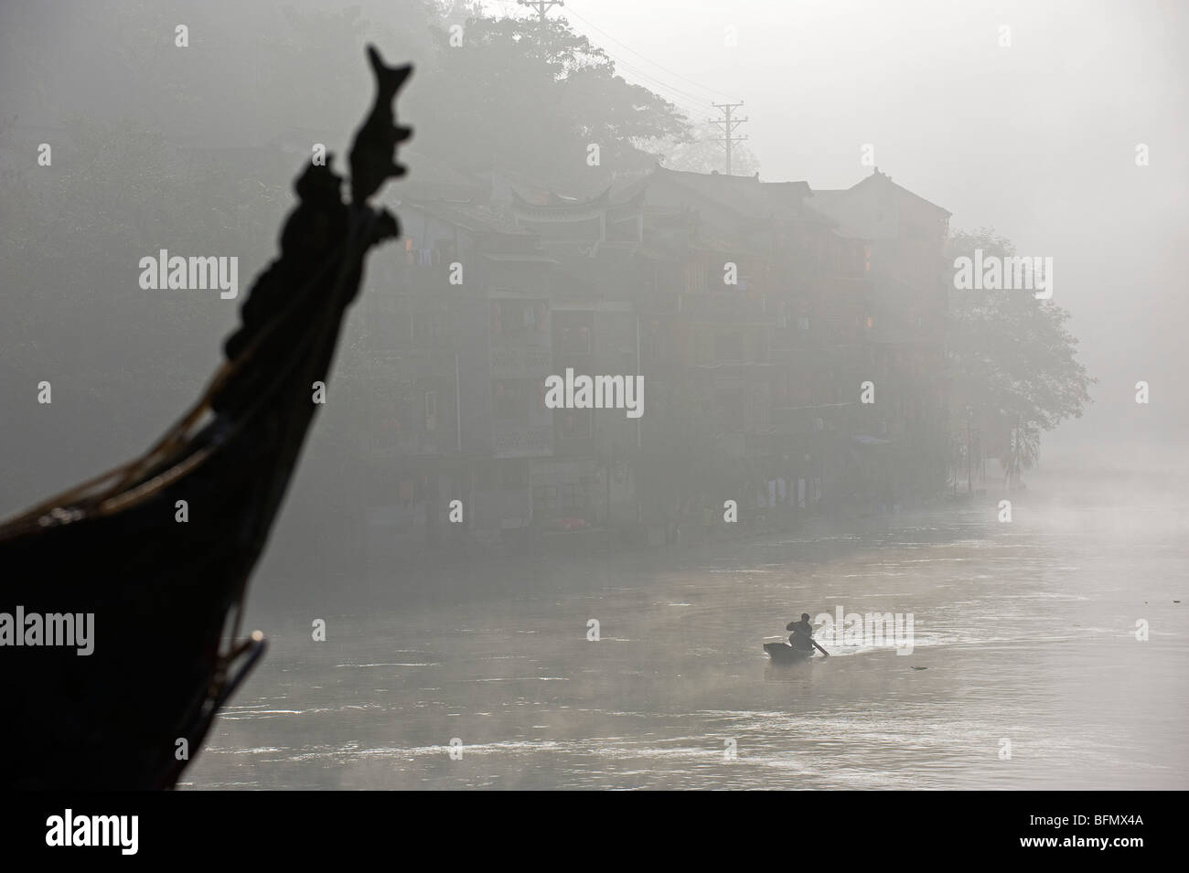 China, Hunan Province, Fenghuang, riverside houses in morning mist ...