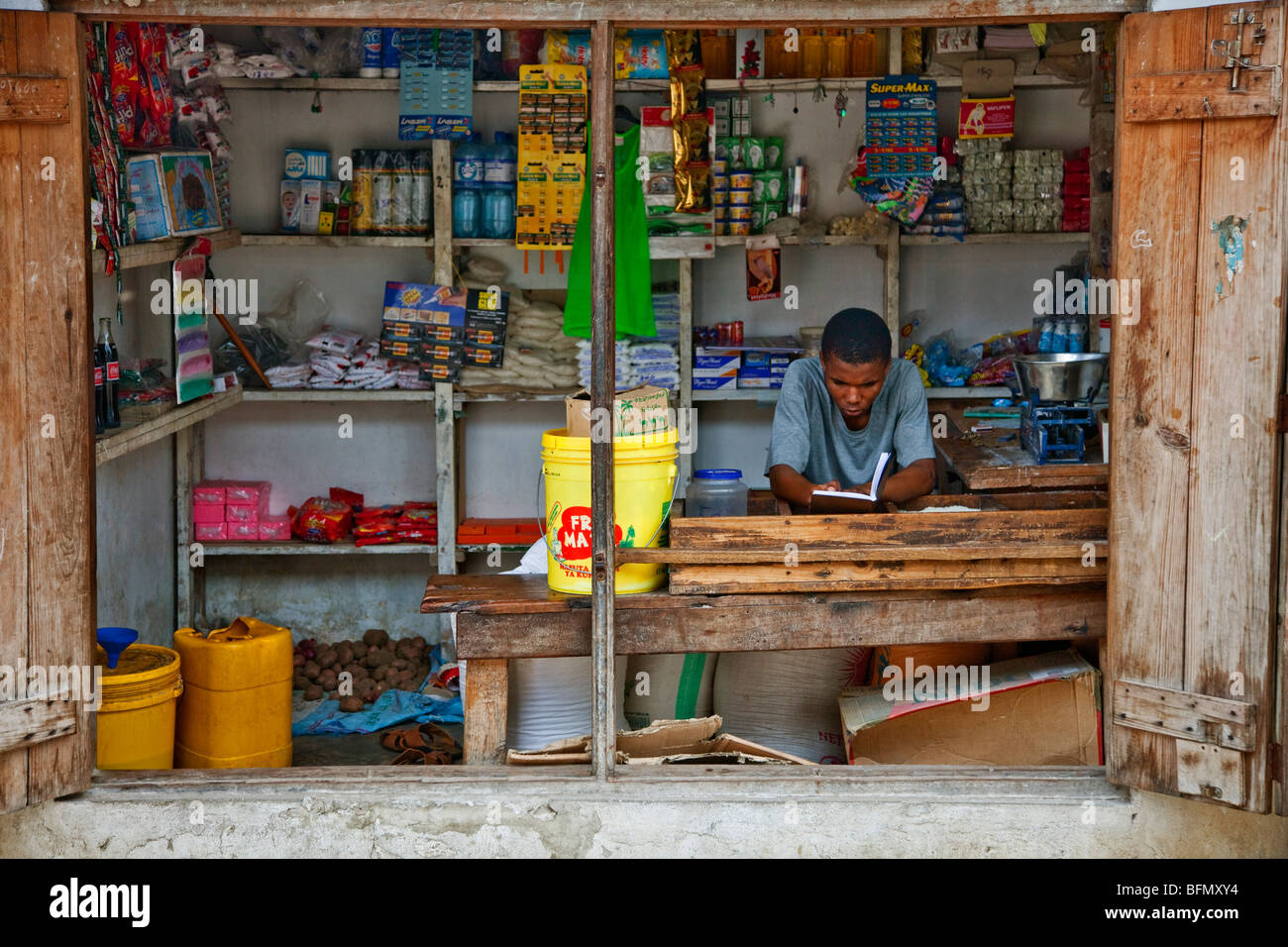 Tanzania, Zanzibar. A shopkeeper reads while waiting for customers at ...