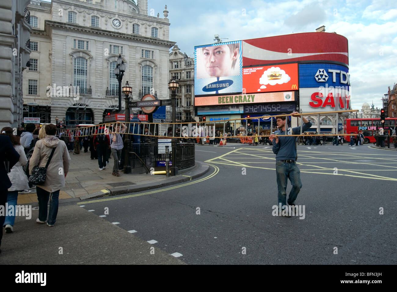 a man with a long ladder crosses the street at picadilly in london ...