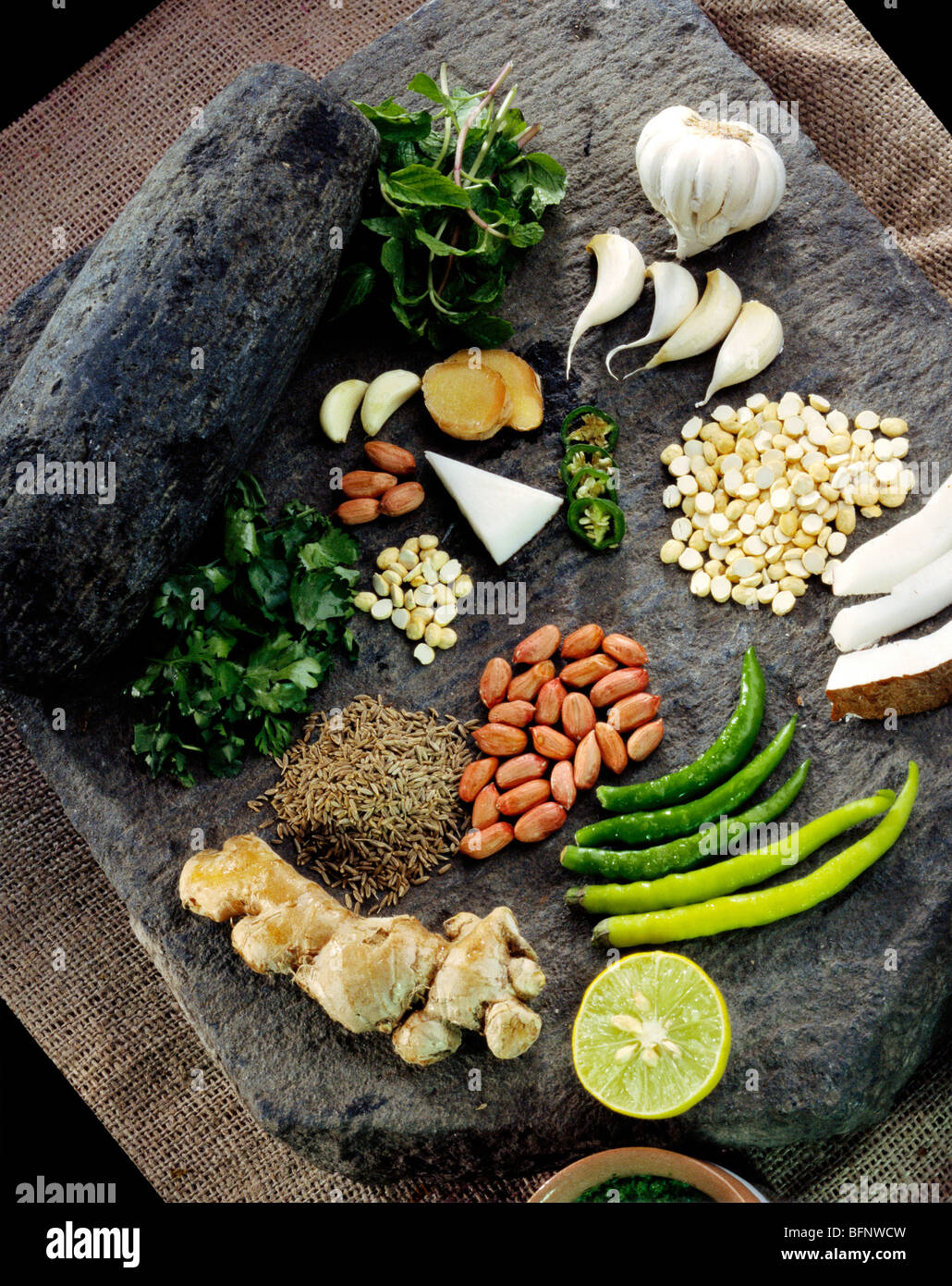 ingredients for green chatni on stone pestle ; garlic lemon ginger ...