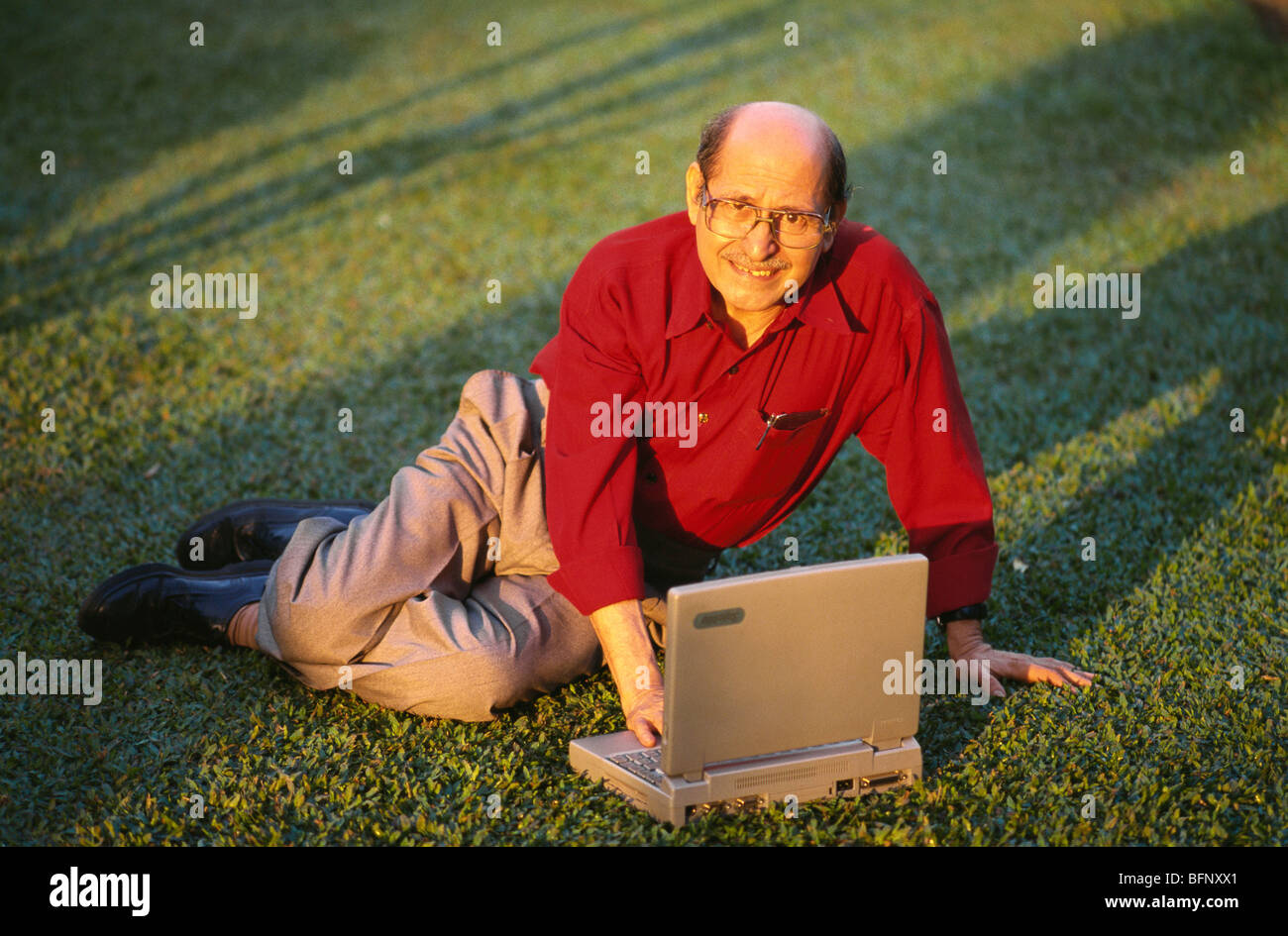 Indian senior man on laptop computer sitting in grass ; MR#307 Stock ...
