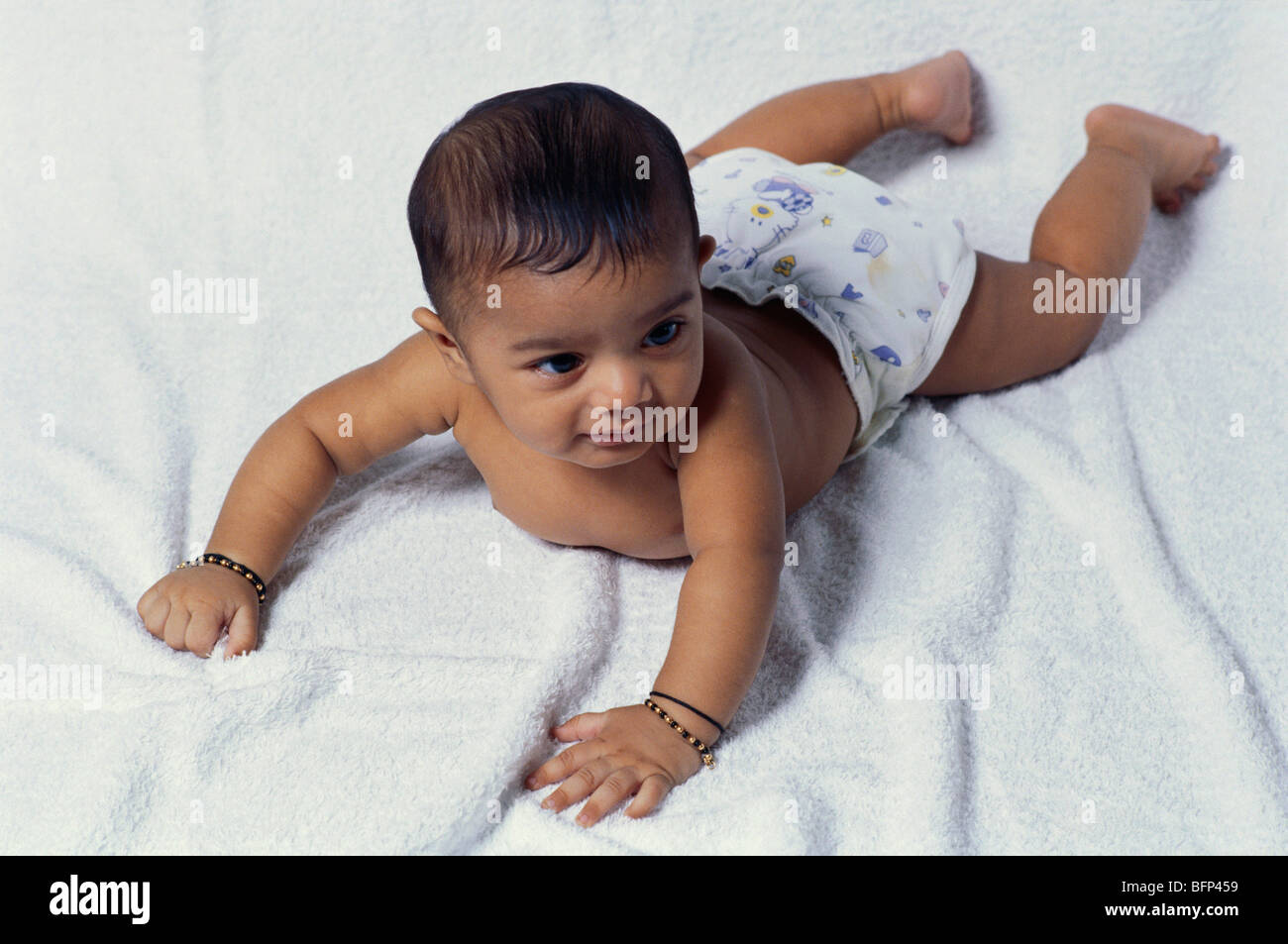 Indian baby on his tummy ; wearing diaper nappy and talisman amulets on ...