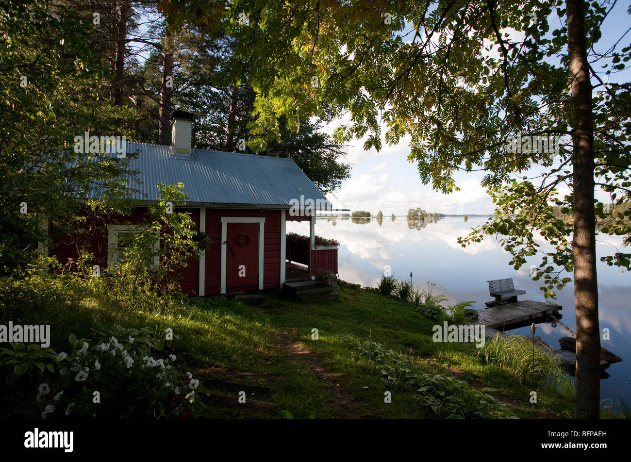 Exterior of a small red wooden sauna cabin by a flat calm lake at ...