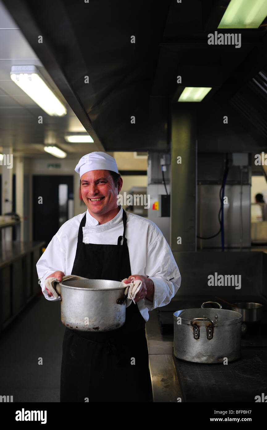 A student chef standing in a college kitchen in uniform, with apron and ...