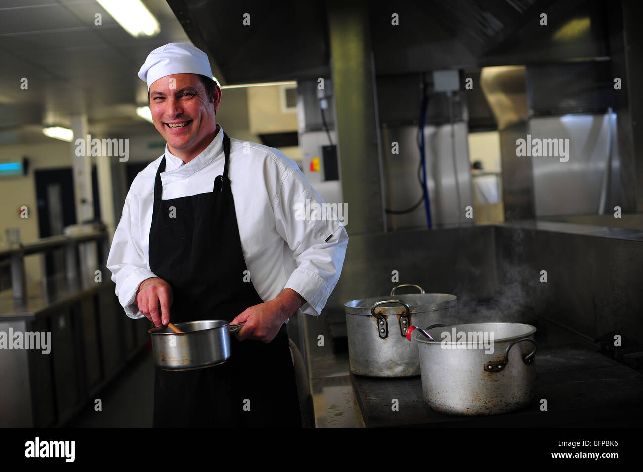 A student chef standing in a college kitchen in uniform, with apron and ...