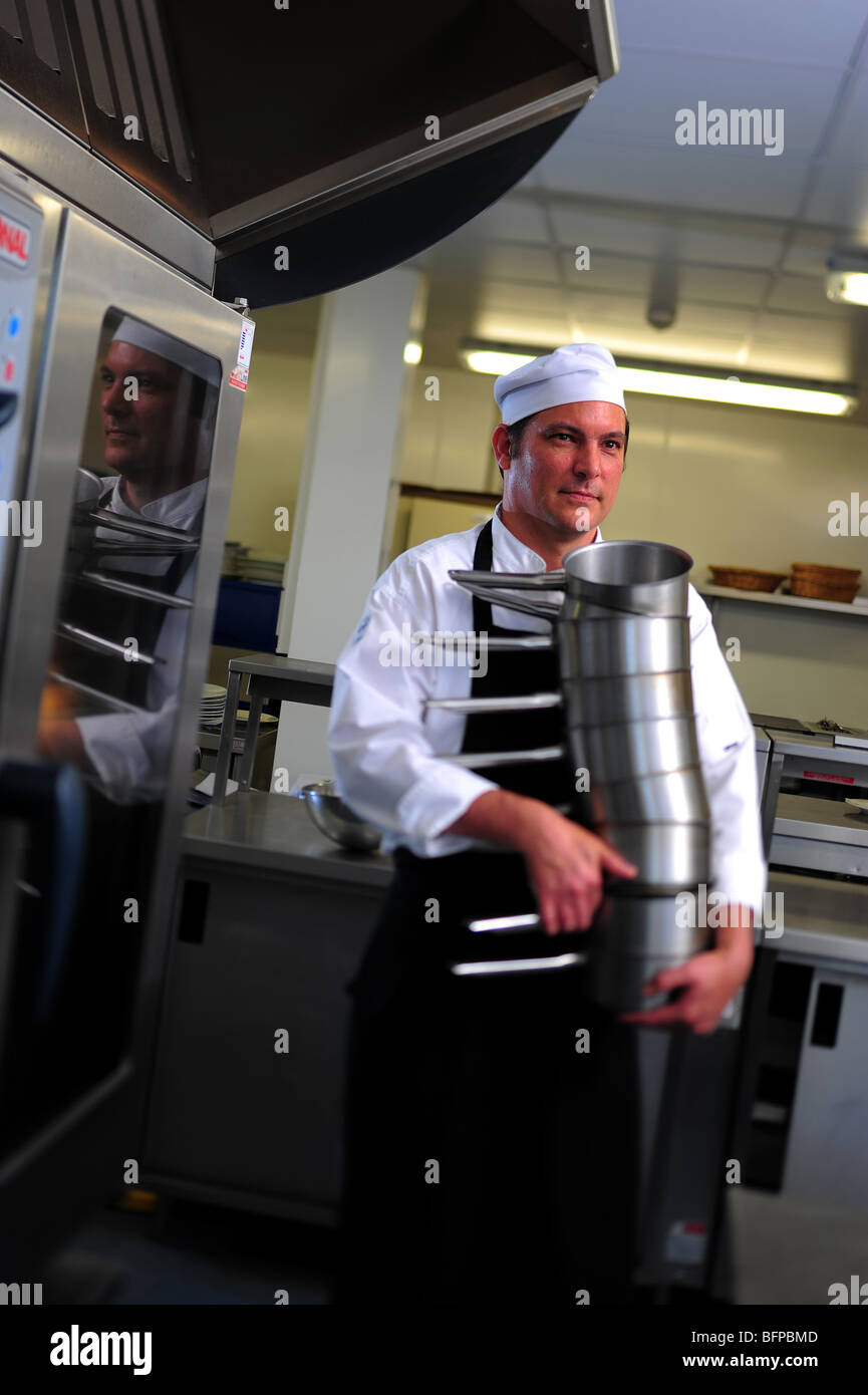 A student chef standing in a college kitchen in uniform, with apron and ...