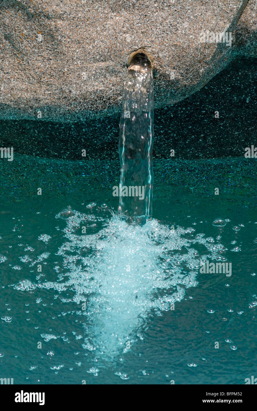 Water flowing from a decorative rock into a plue pool with bubbles ...