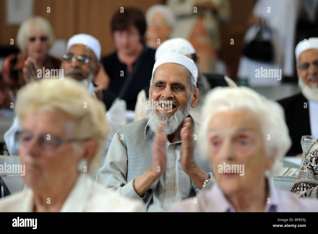A mixed multi-cultural group of elderly people exercise in their chairs ...