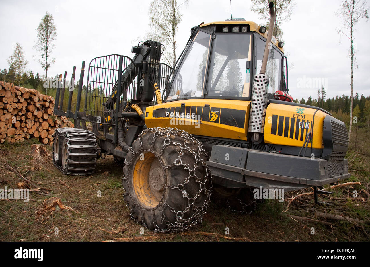Pile of pine logs and Finnish Ponsse Elk forest harvester / forwarder ...