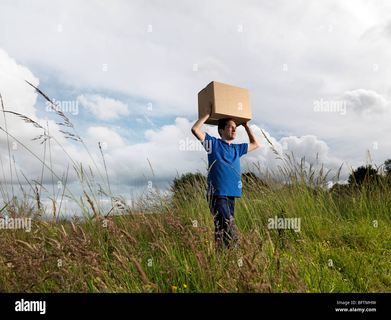 man carrying boxes through field Stock Photo - Alamy
