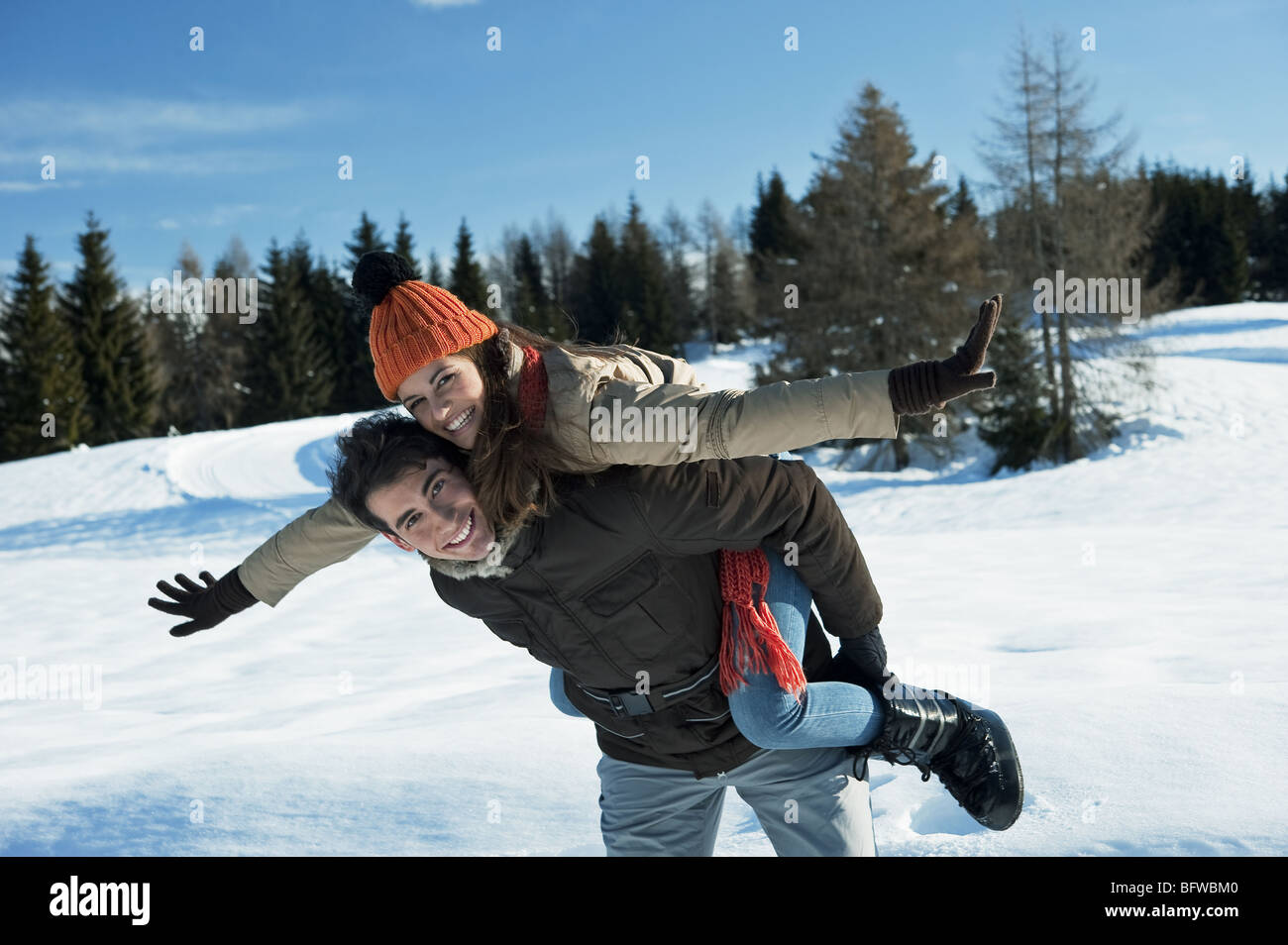 Young woman riding piggyback on young man in winter scene Stock Photo ...