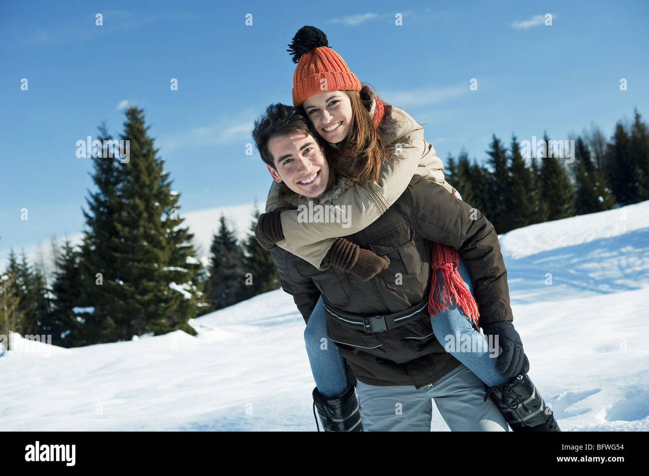 Young woman riding piggyback on young man in winter scene Stock Photo ...