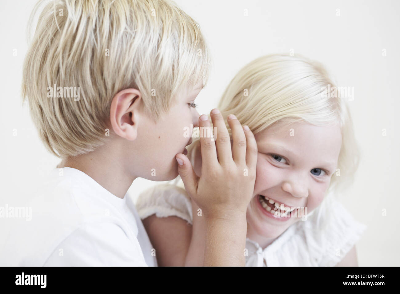Young boy whispering into girl's ear Stock Photo - Alamy