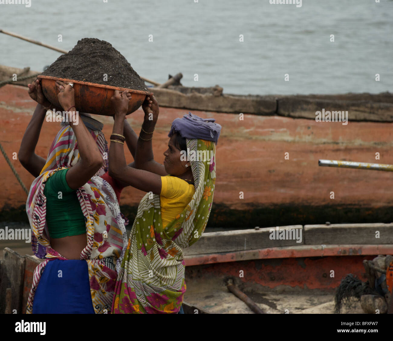Female workers carry loads of sand and grit from mining boats on the ...