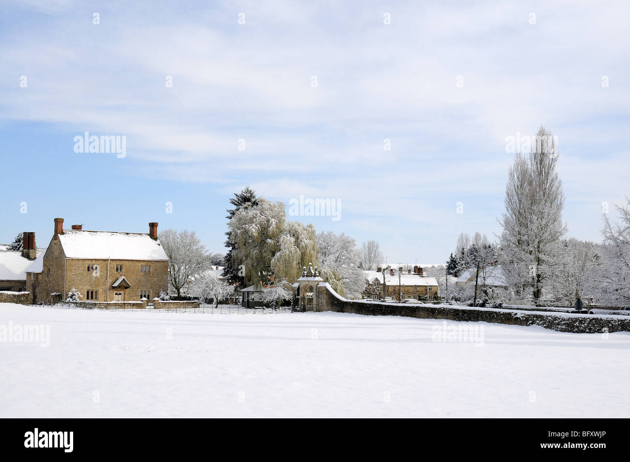 Manor house in the Cotswolds covered in snow with a village behind ...