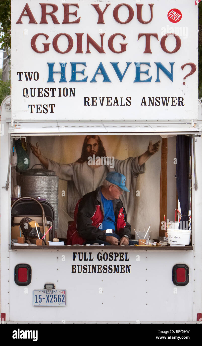 A man sits in a booth at a State Fair. The booth is titled "Are You ...