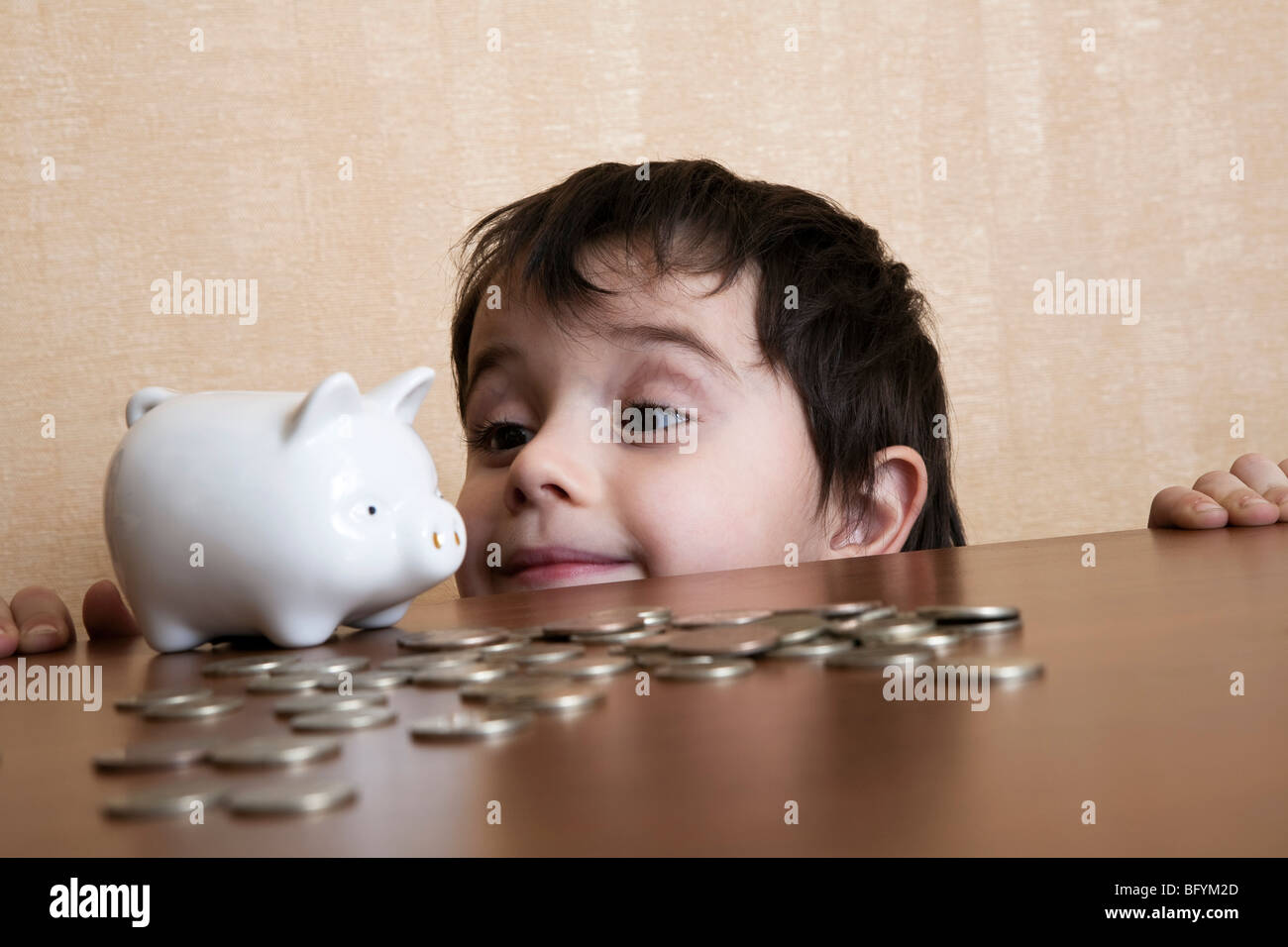 young boy behind table looking at piggybank Stock Photo - Alamy