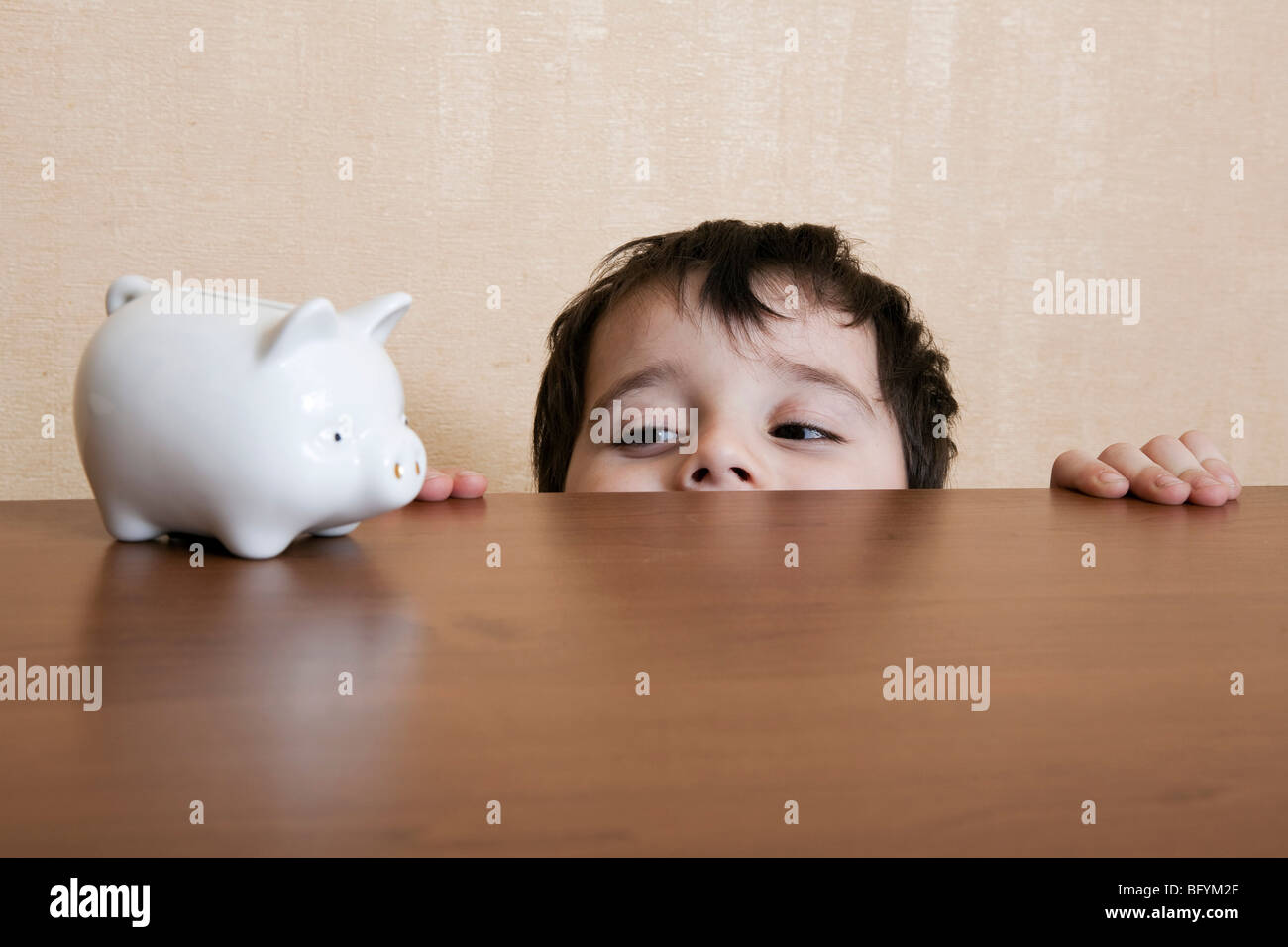 young boy behind table looking at piggybank Stock Photo - Alamy