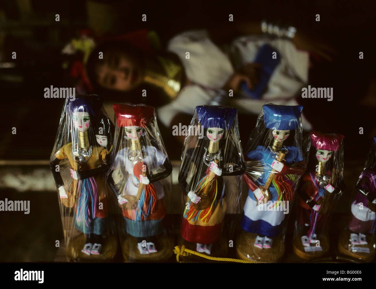 A young long neck Pa Dong Tribe girl rests in a small shop behind some ...