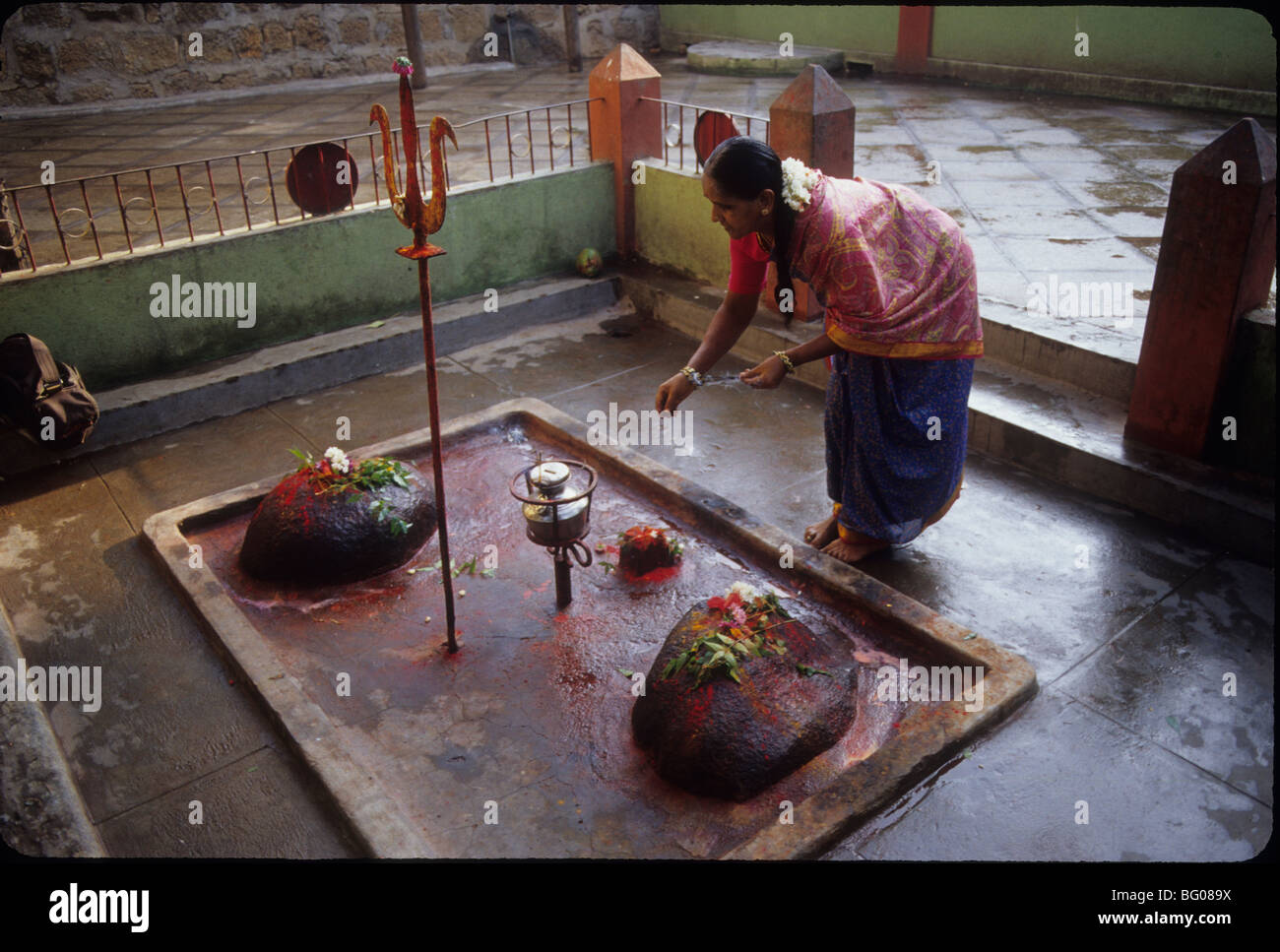 A Hindu woman bows in front of a trident in a small Hindu shrine in ...