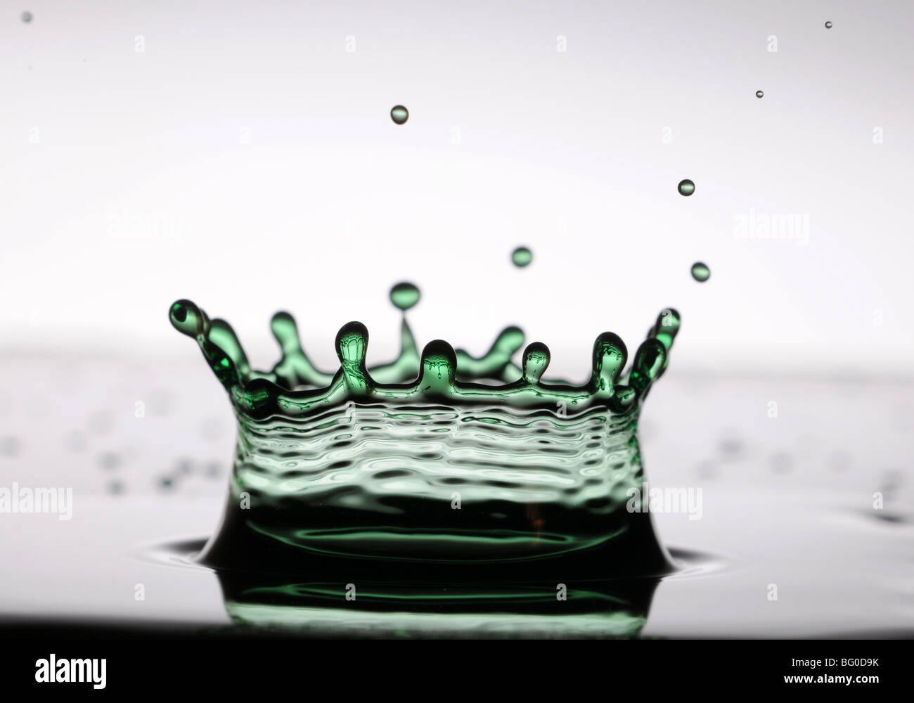 A drop of green water forming a coronet as it splashes into a shallow ...