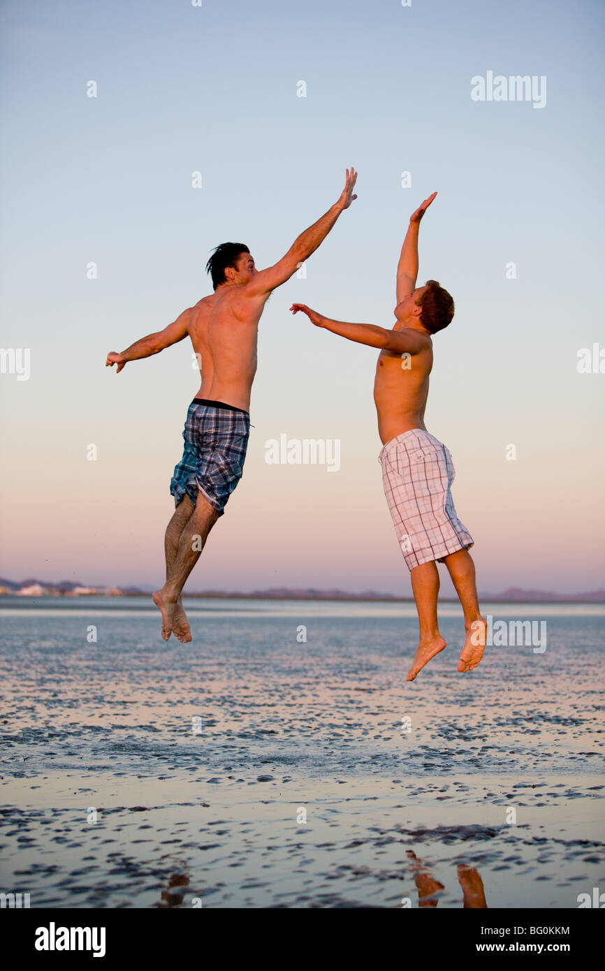 Young men leap in the air and "high five" on the beach Stock Photo - Alamy