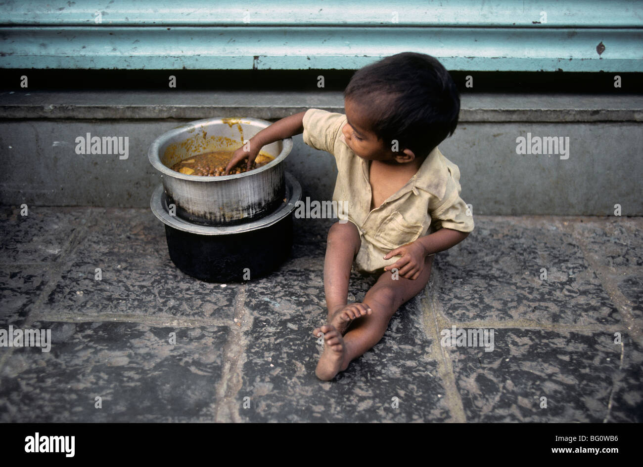 A young boy has his breakfast of beans on a sidewalk in Mumbai, India ...