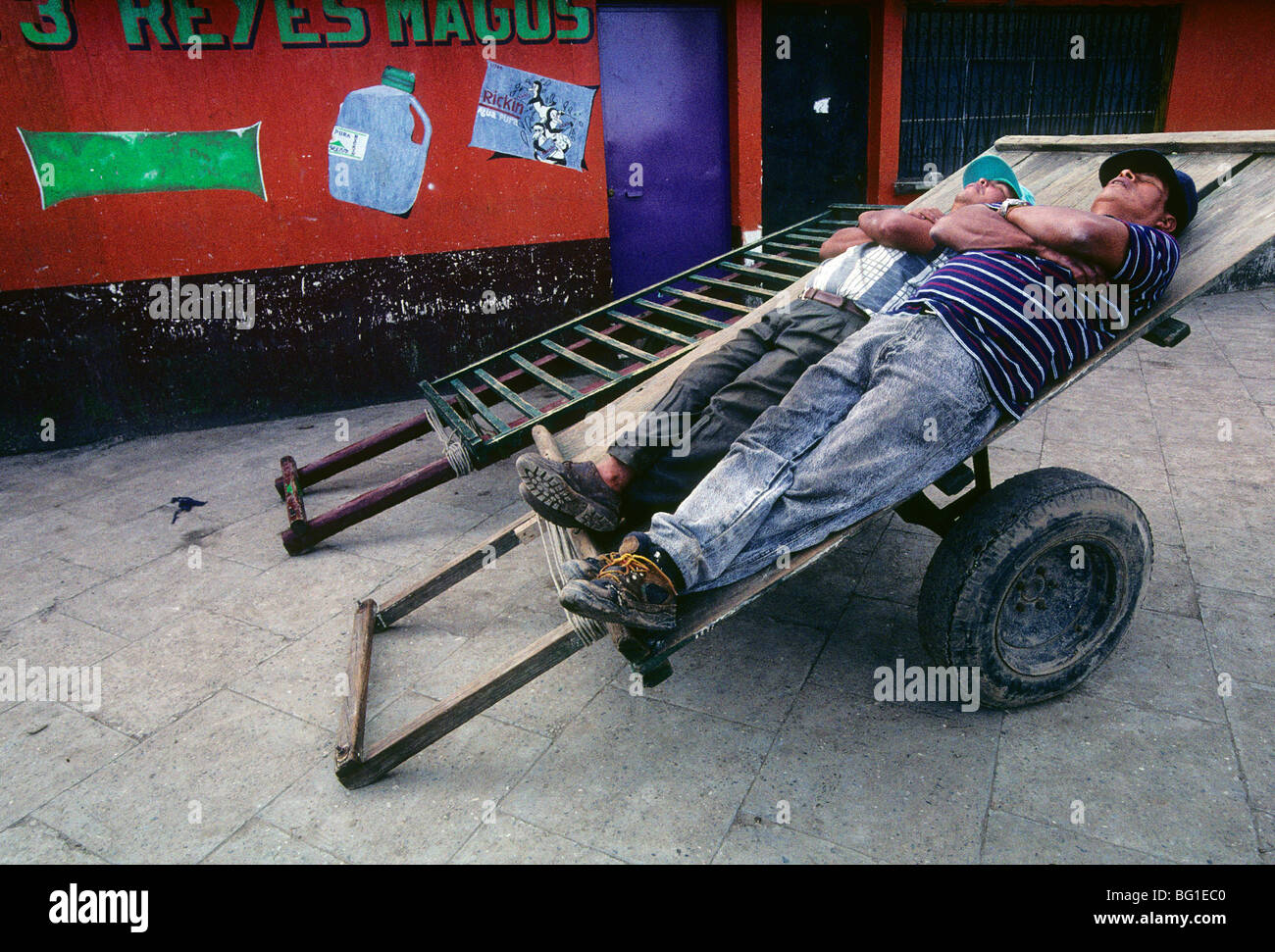 Two men take a nap on a push cart in the bus station parking lot in ...