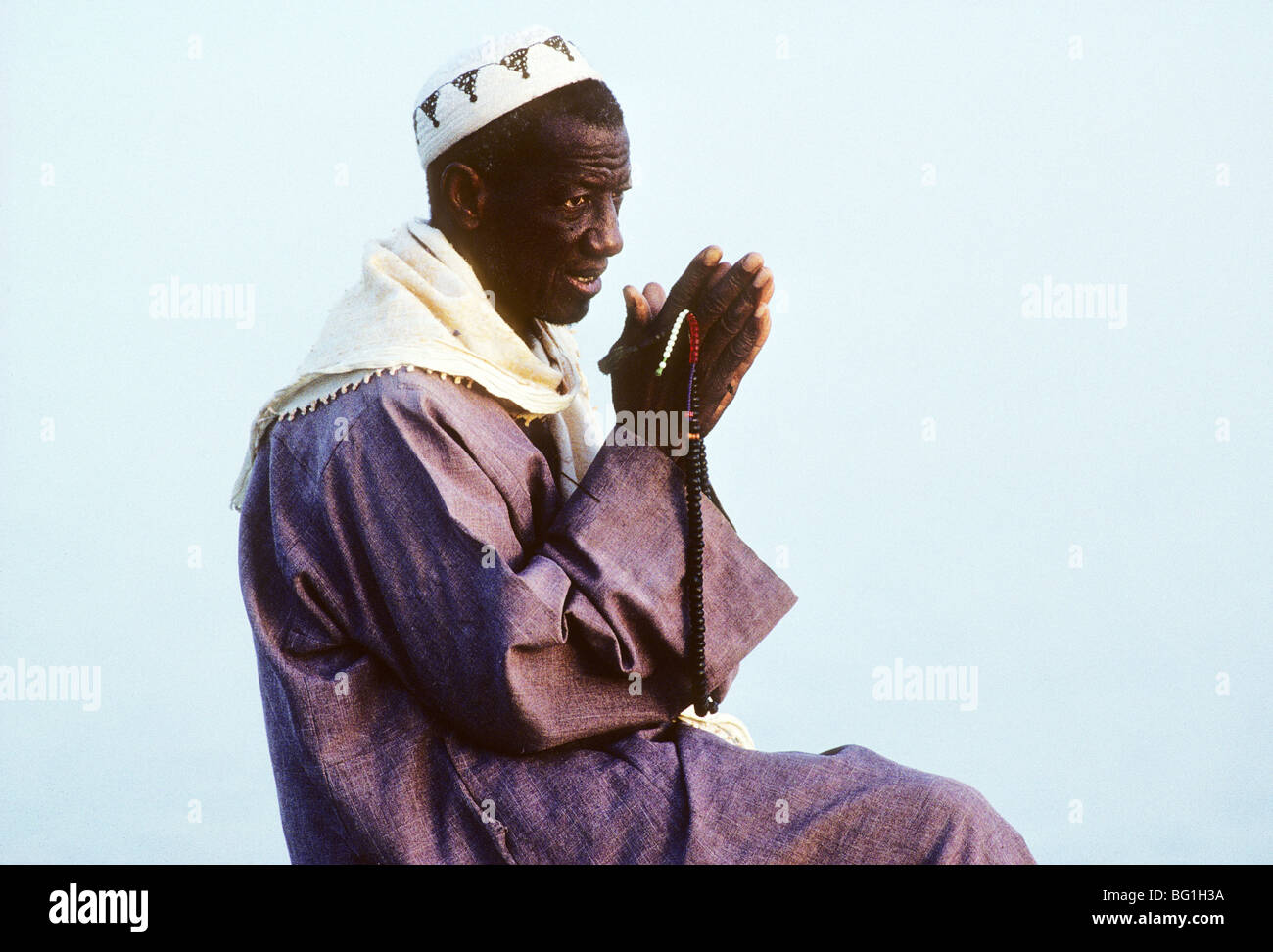 A Muslim man holding prayer beads prays at the Niger River first thing ...