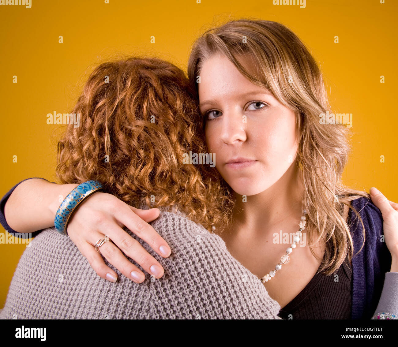 Two women giving each other a hug. One is looking at the viewer with ...