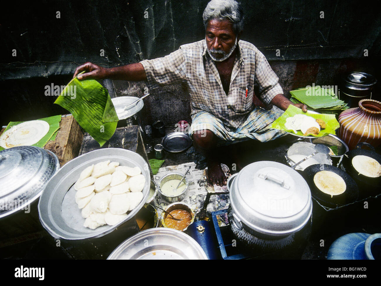A man making idly at an outdoor food stall in Madurai, India. Idly is a ...