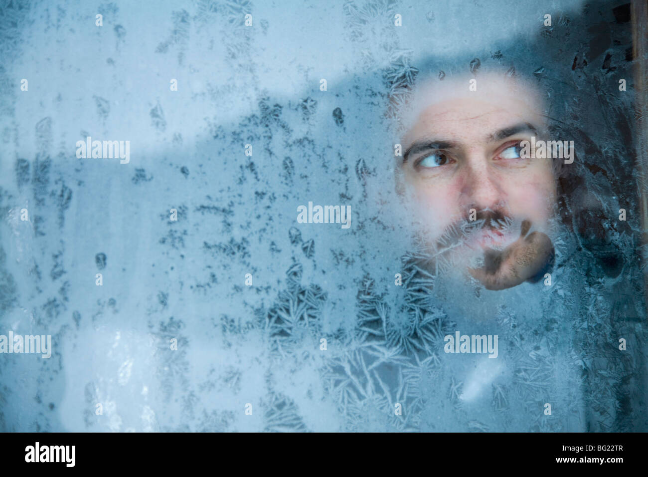 Young man looking out a frosted window Stock Photo - Alamy