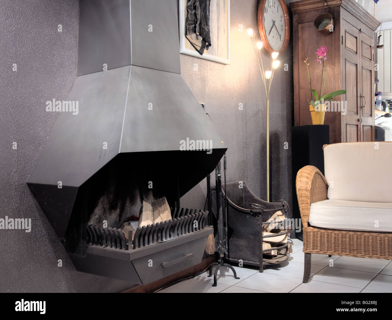 Home interior with fire place, armchair and logs. Clock and orchid on ...