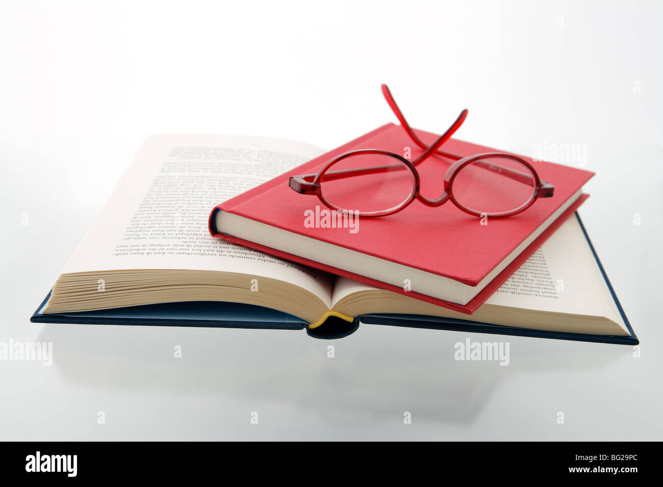 red and blue books with reading glasses on a reflecting white ...