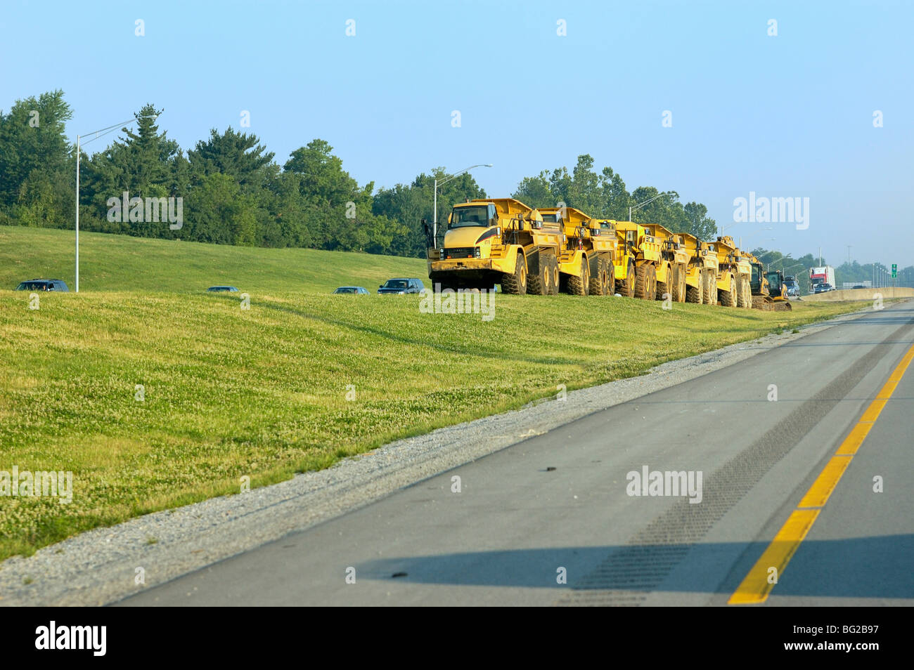 A line of road construction trucks parked on side of highway Stock ...