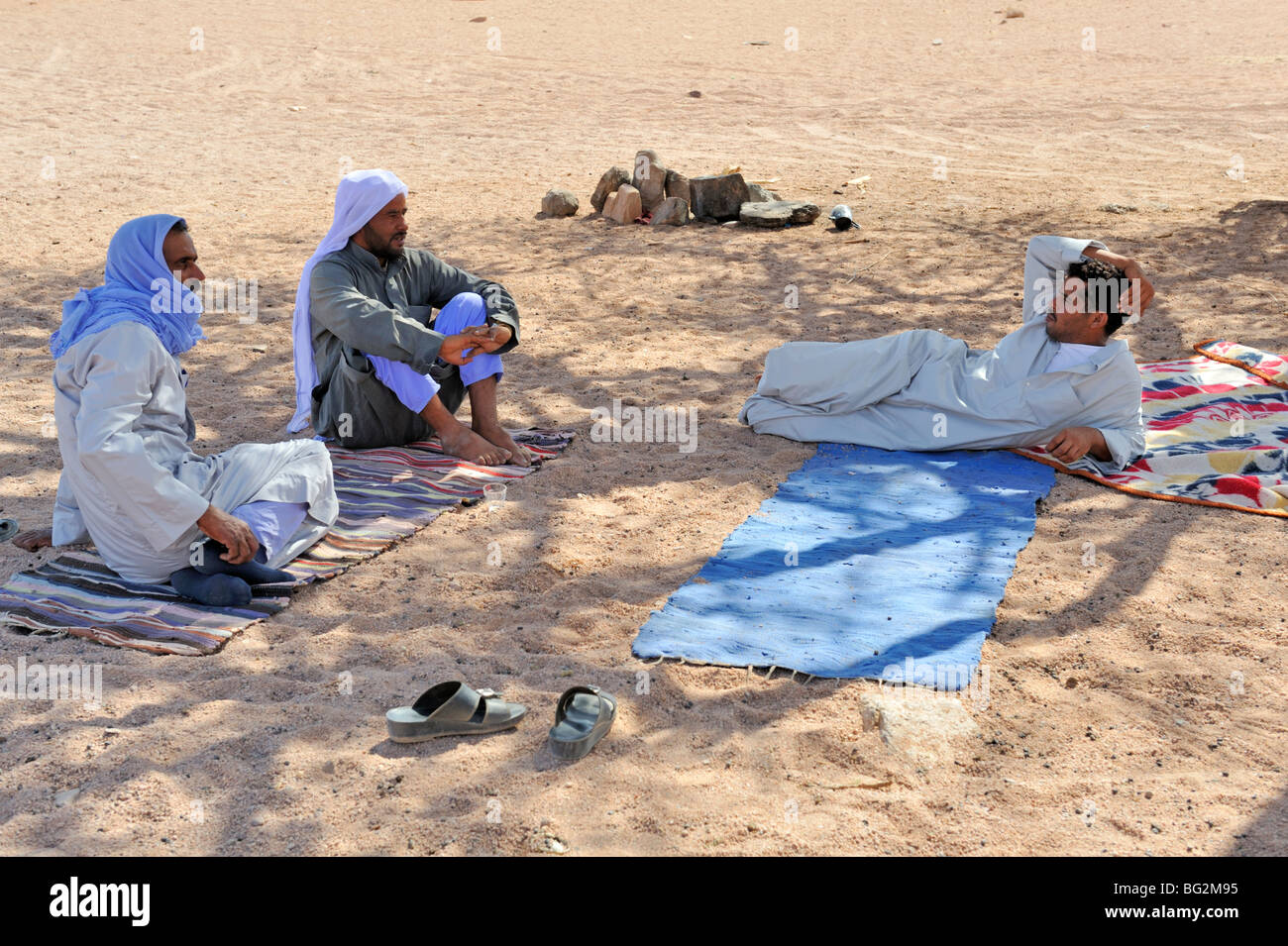 Three Bedouin Arab men relaxing on tradition blankets in shadow of tree ...