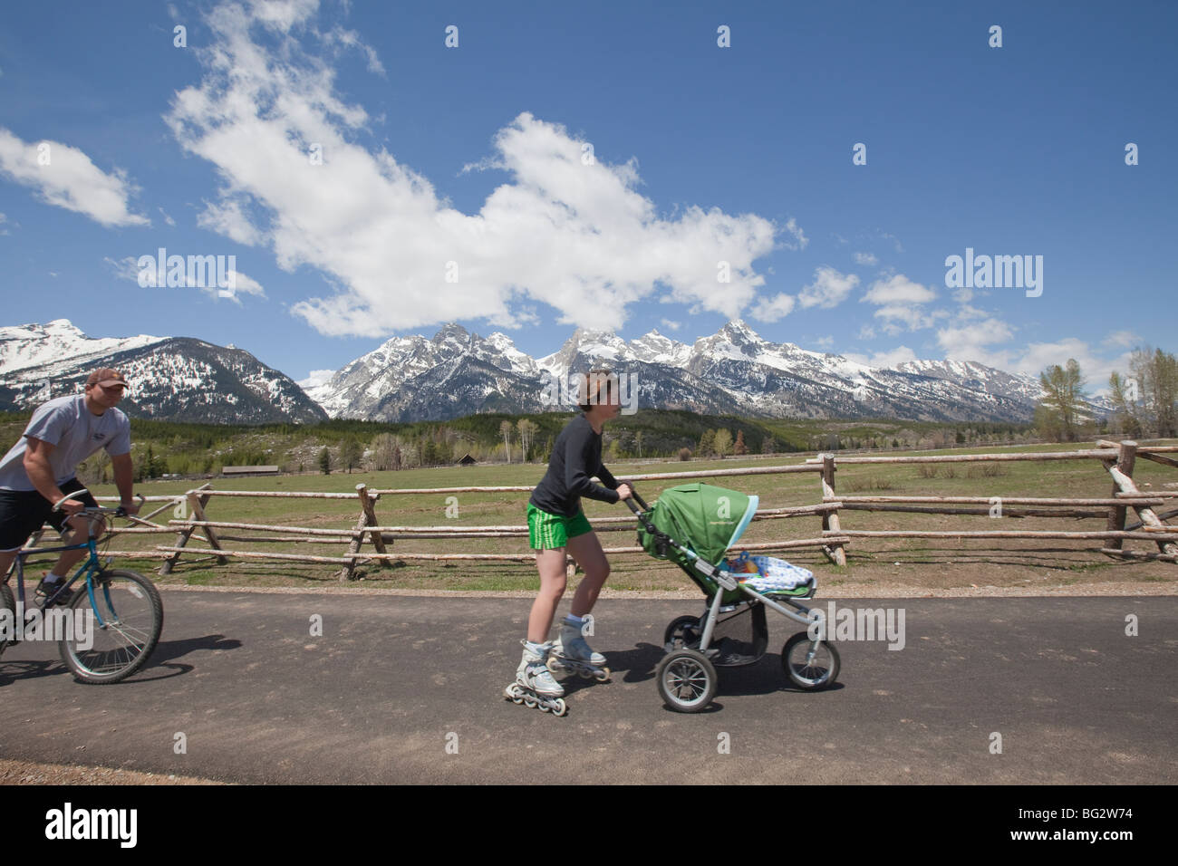 Biker and rollerblading parent pushing stroller enjoy paved bike trail ...