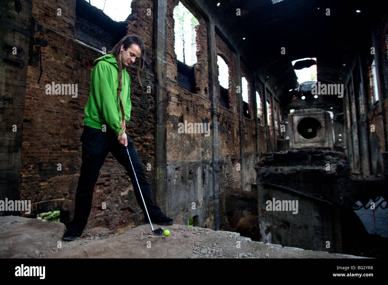 Young man with dreadlocks playing off golf in post industrial hall ...
