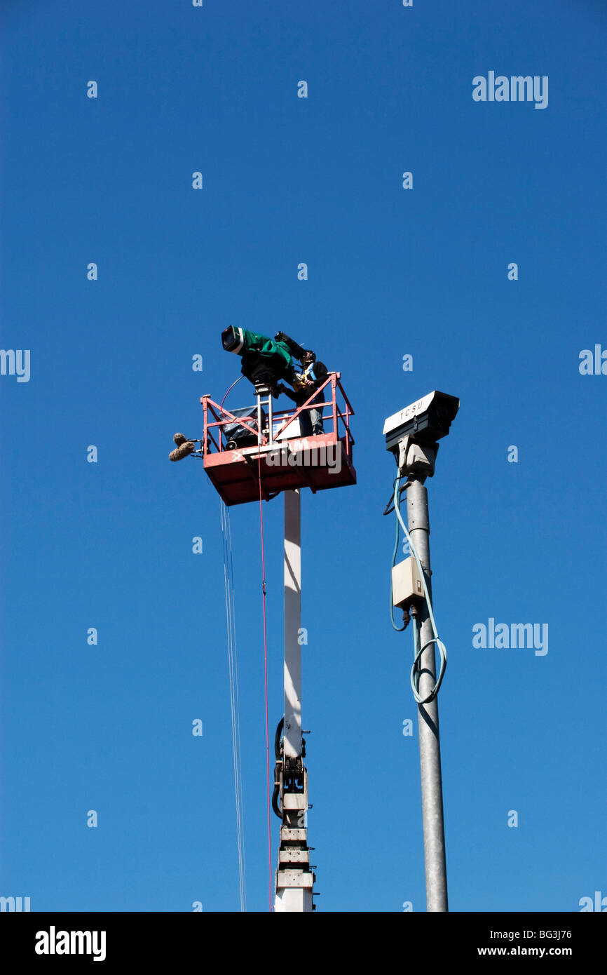 TV camera man filming from atop a crane beside a security CCTV camera ...