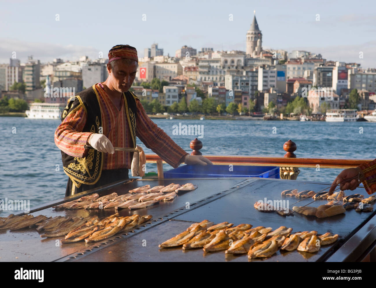 Man cooking fish on a boat on the Golden Horn with the Galata Tower and ...