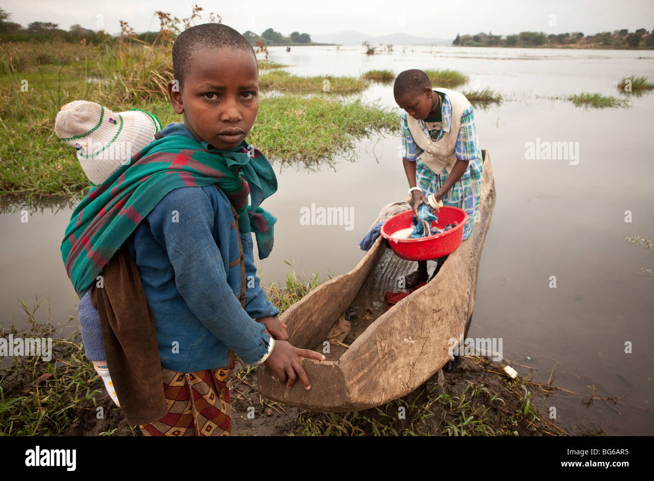 A girl with a baby stands along the shores of Lake Babati in Central ...