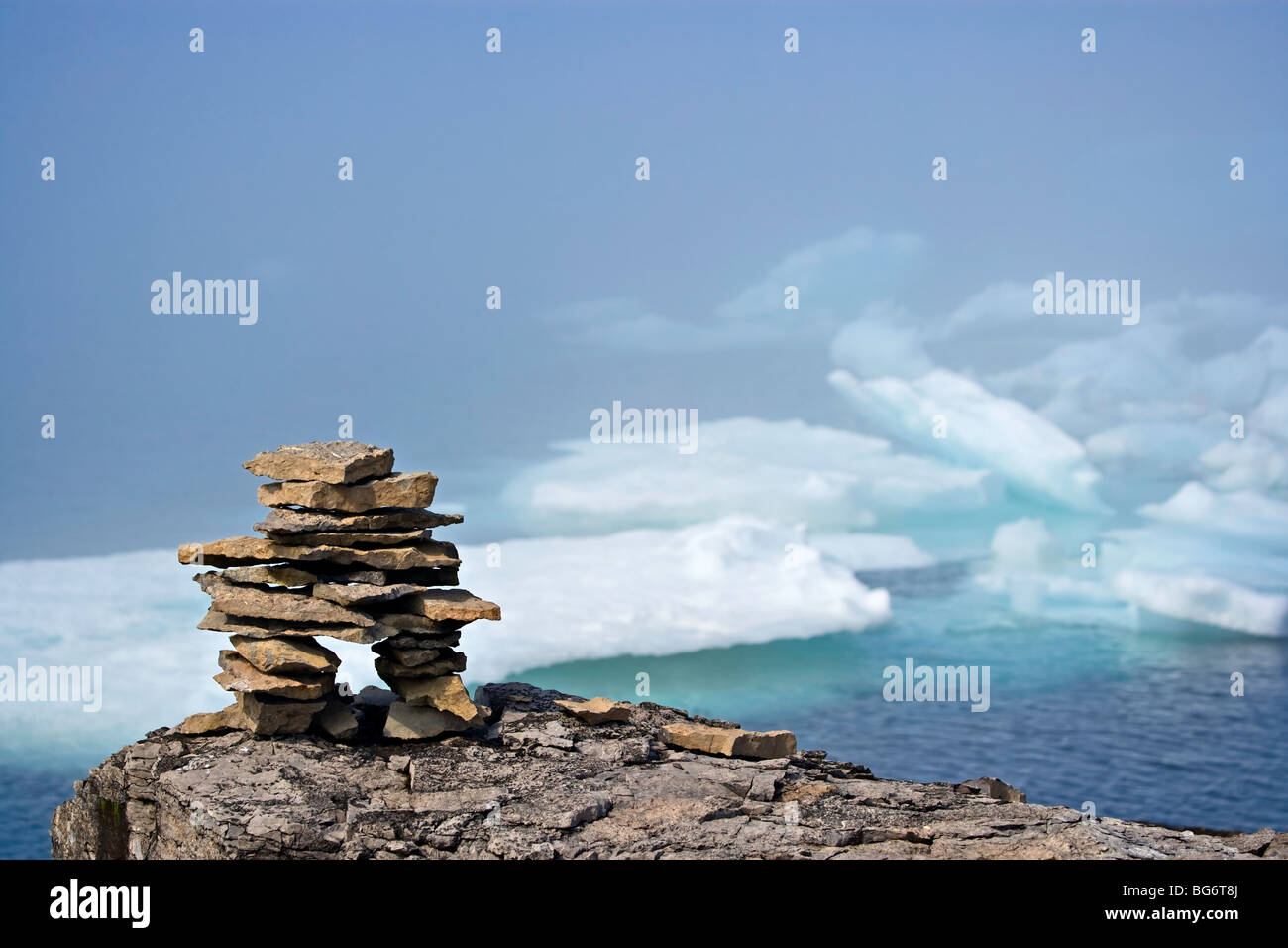 Rock inukshuk on a ledge backdropped by pack ice veiled by fog in the ...