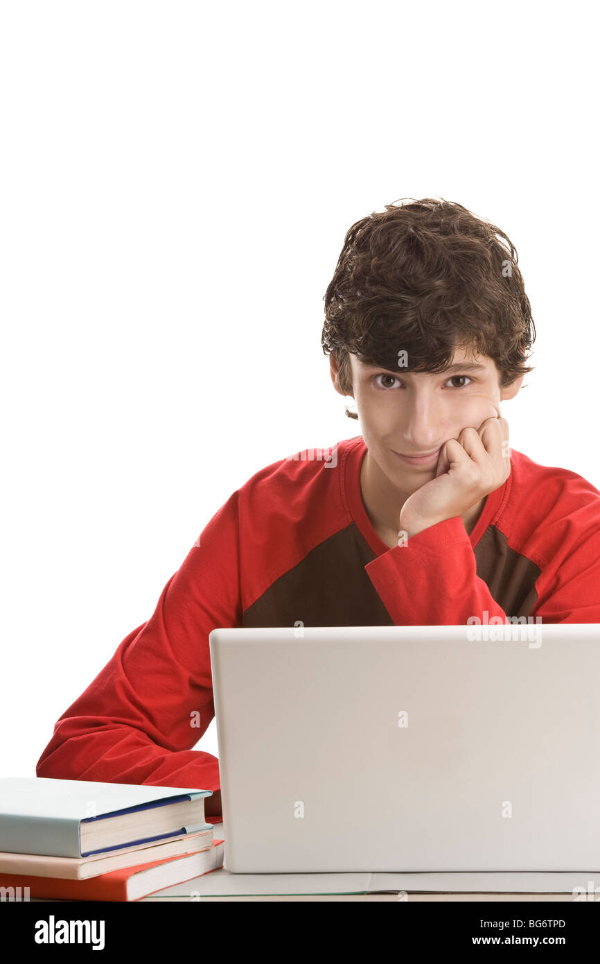 Teenage boy sitting behind desk with laptop computer isolated on white ...
