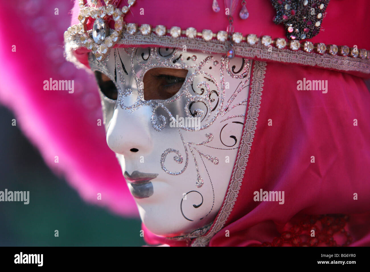 Close-up of a Venetian woman wearing a white mask and pink costume in ...
