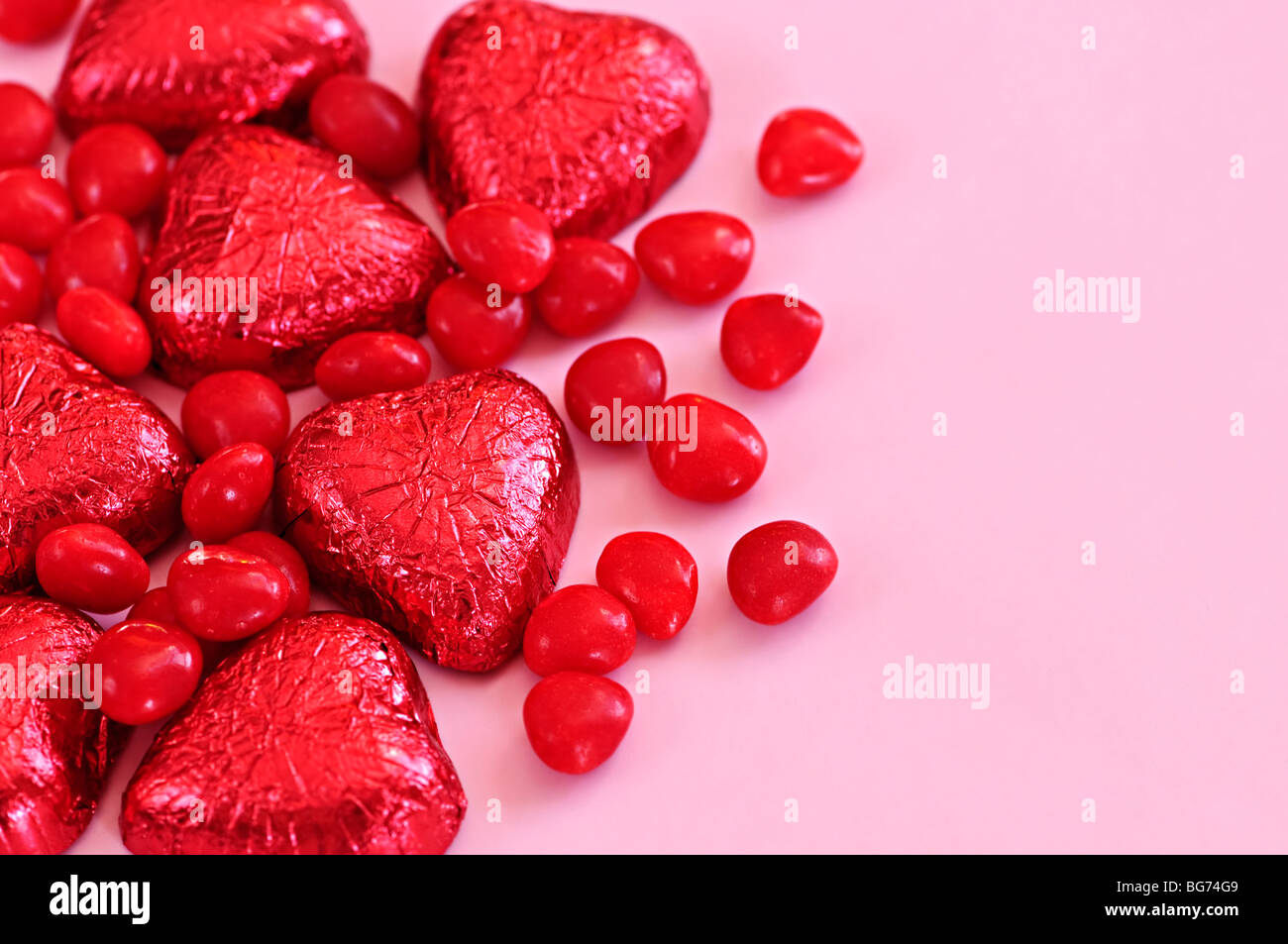 Red Valentine's candies and foil wrapped chocolates on pink background ...