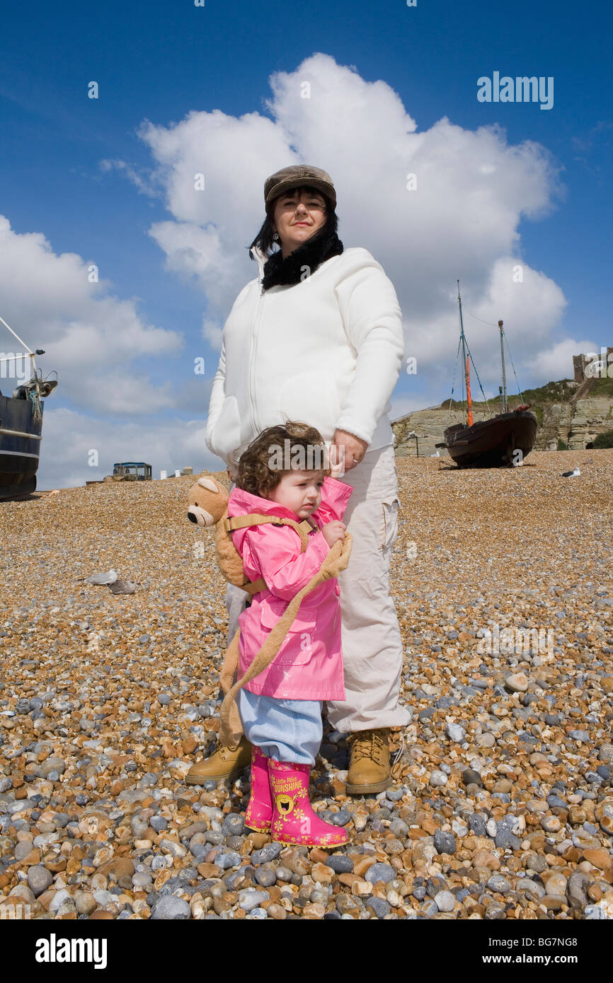 A mother and her daughter wearing a pink mac coat on a pebble beach on ...