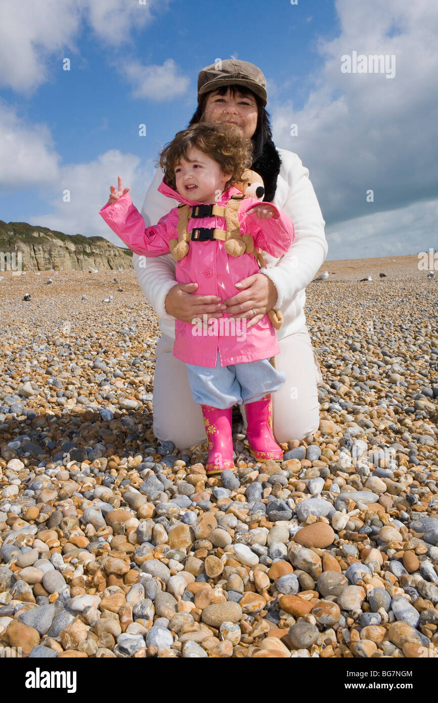 A mother and her daughter wearing a pink mac coat on a pebble beach on ...
